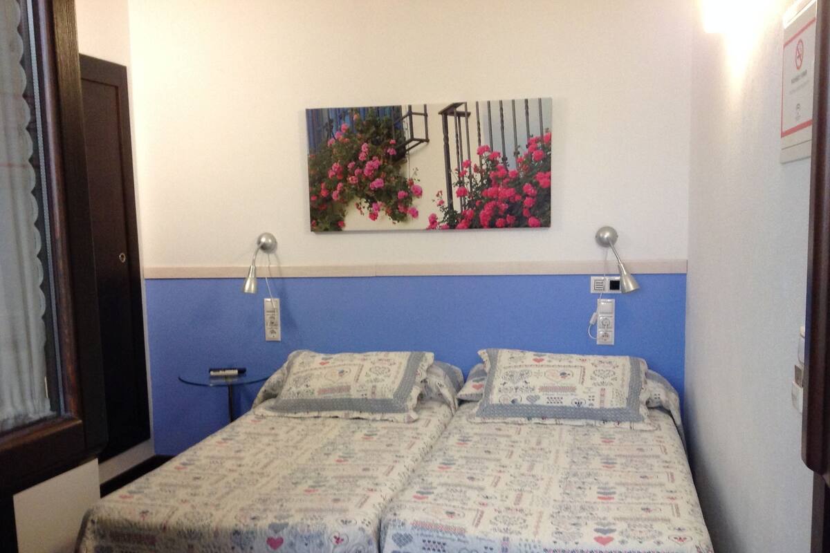 Quarto com duas camas, pintura de flores na parede e esquema de cores azul e branco.