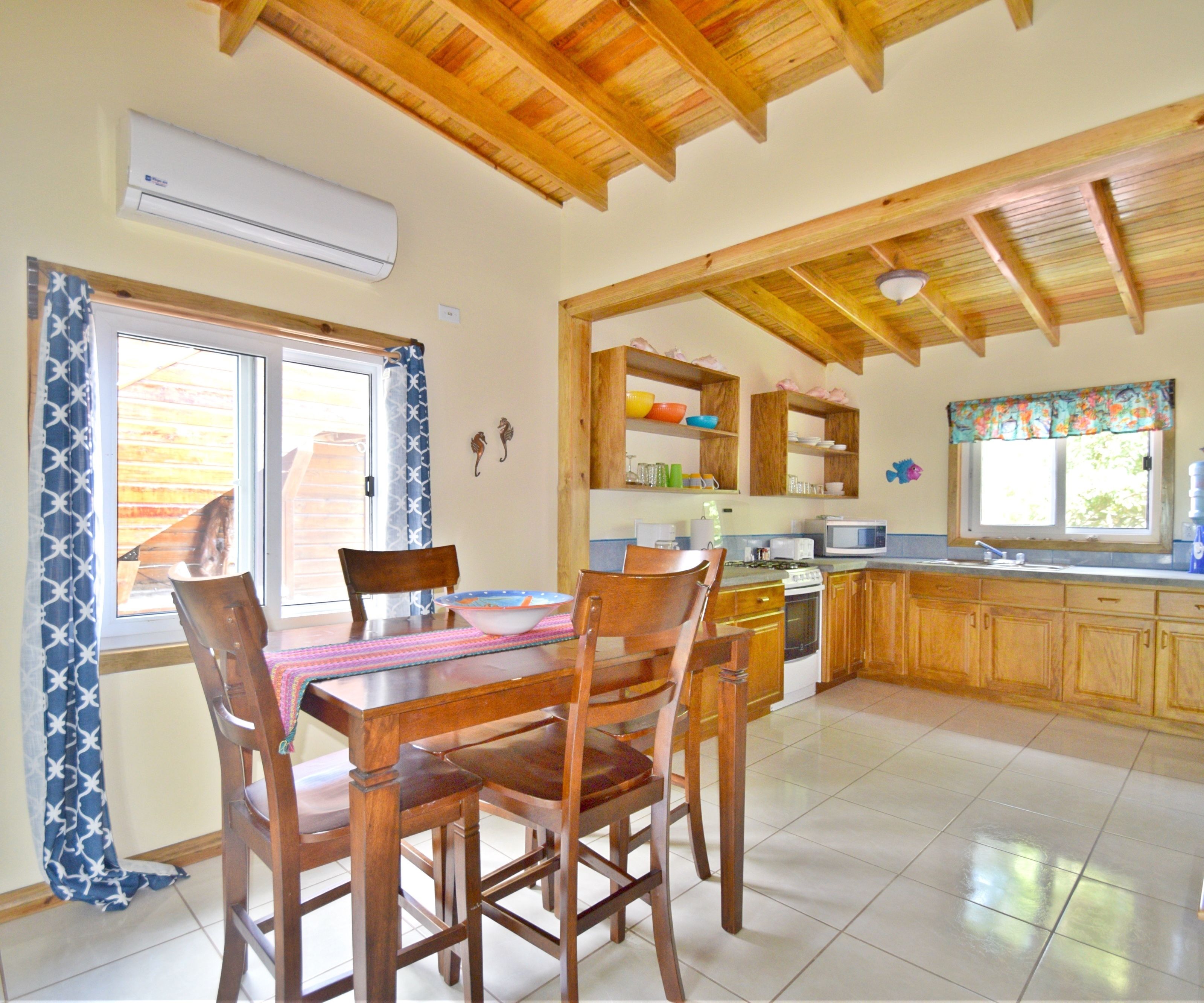 Cozinha com armários de madeira, mesa de jantar com cadeiras e janela com cortinas.