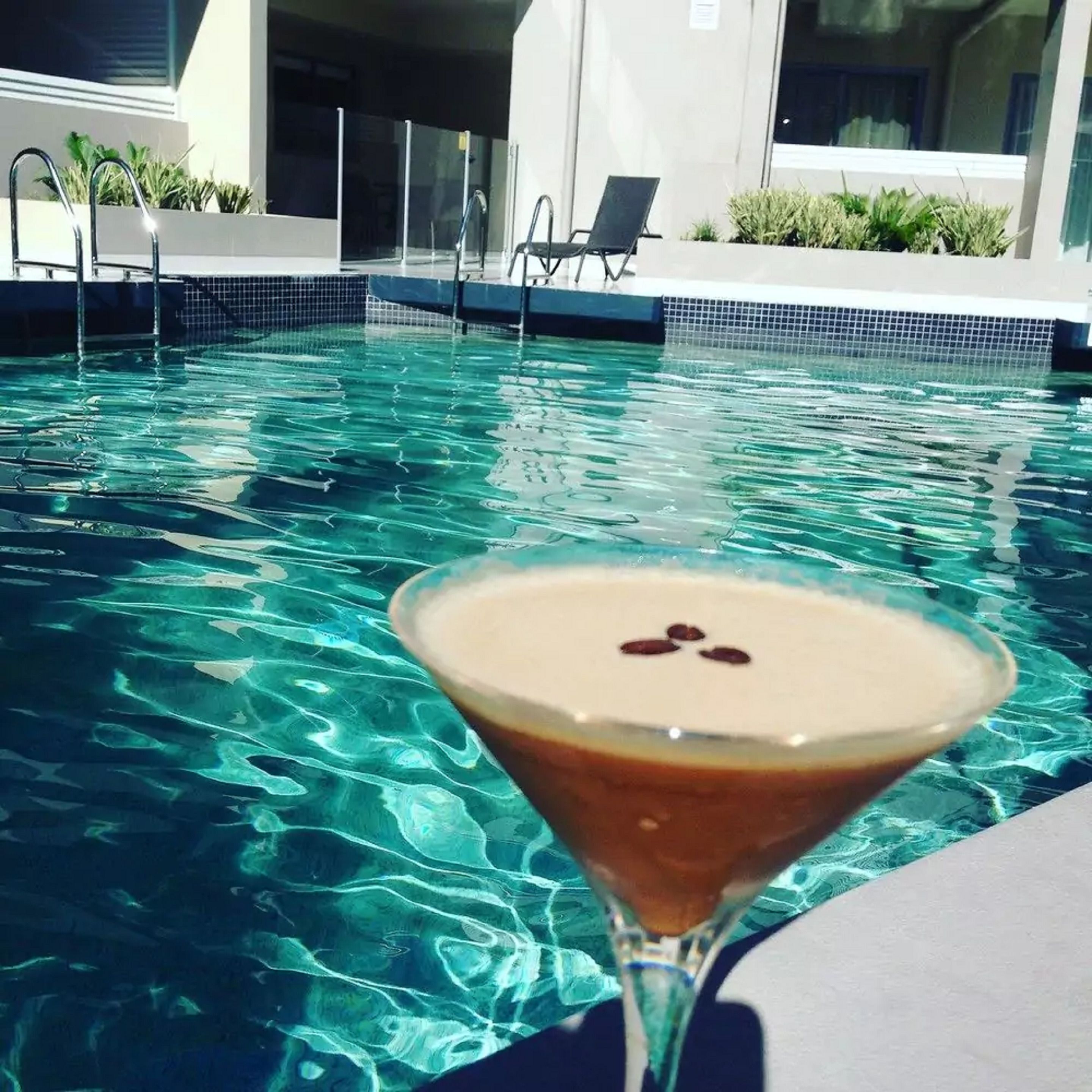 Piscina límpida com um copo de martini em primeiro plano.