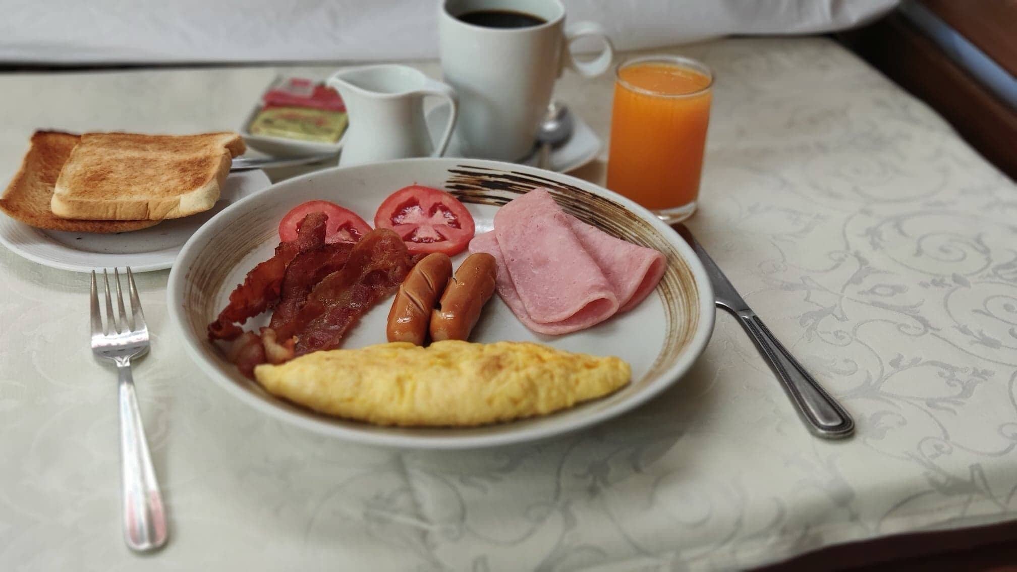 Uma bandeja de café da manhã com torradas, bacon, salsichas, presunto, tomates e um ovo mexido.