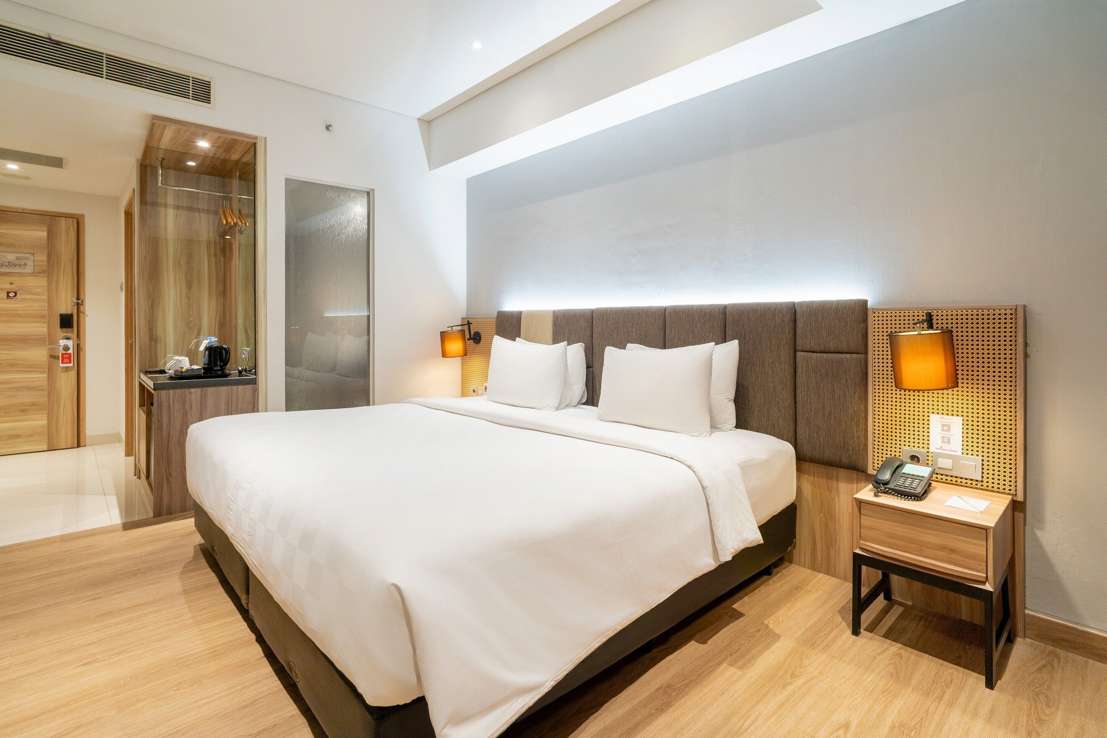 Quarto de hotel moderno com uma cama grande, abajures, uma mesinha com telefone e um espelho.