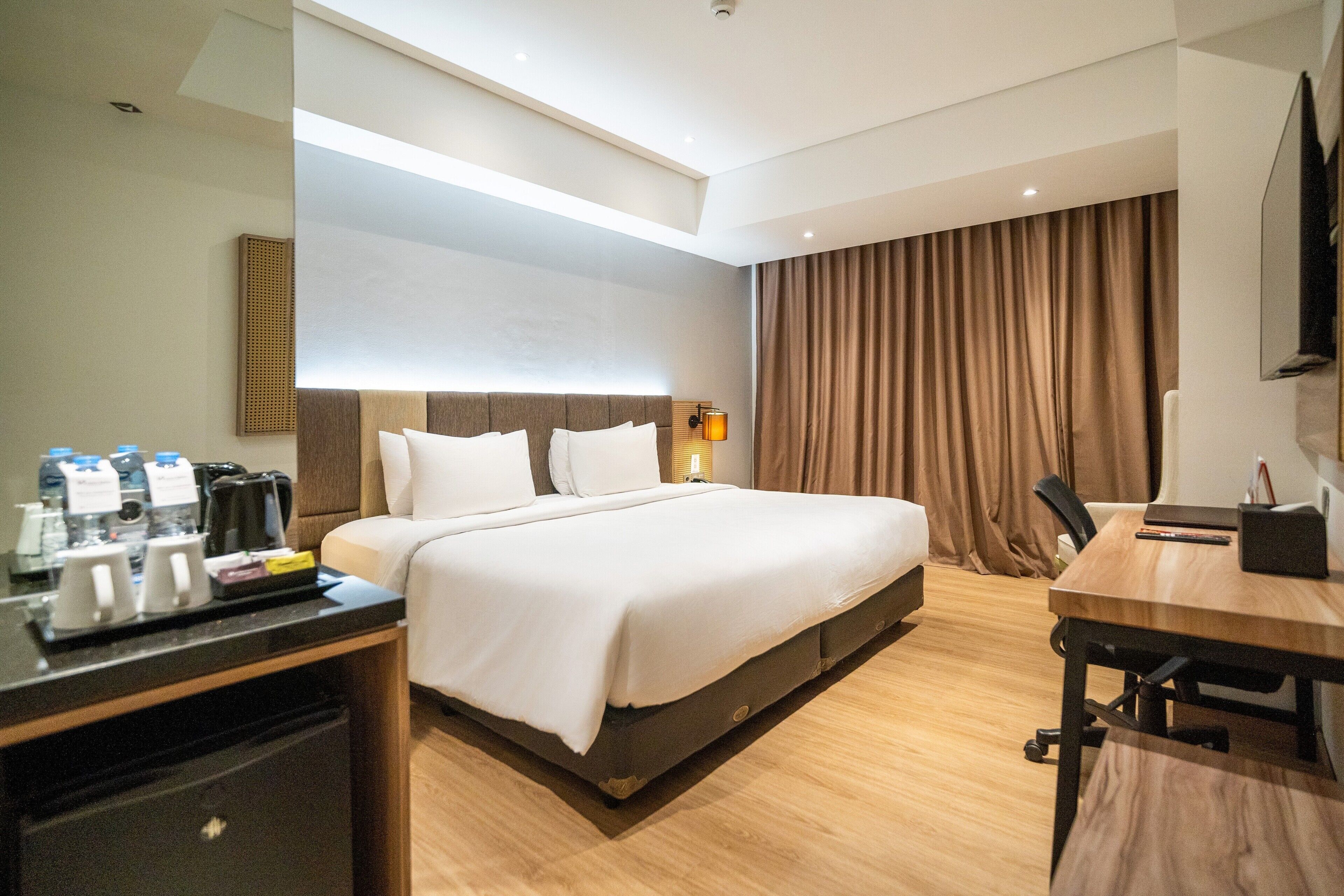 Quarto de hotel moderno com cama, escrivaninha e pequena área de cozinha.