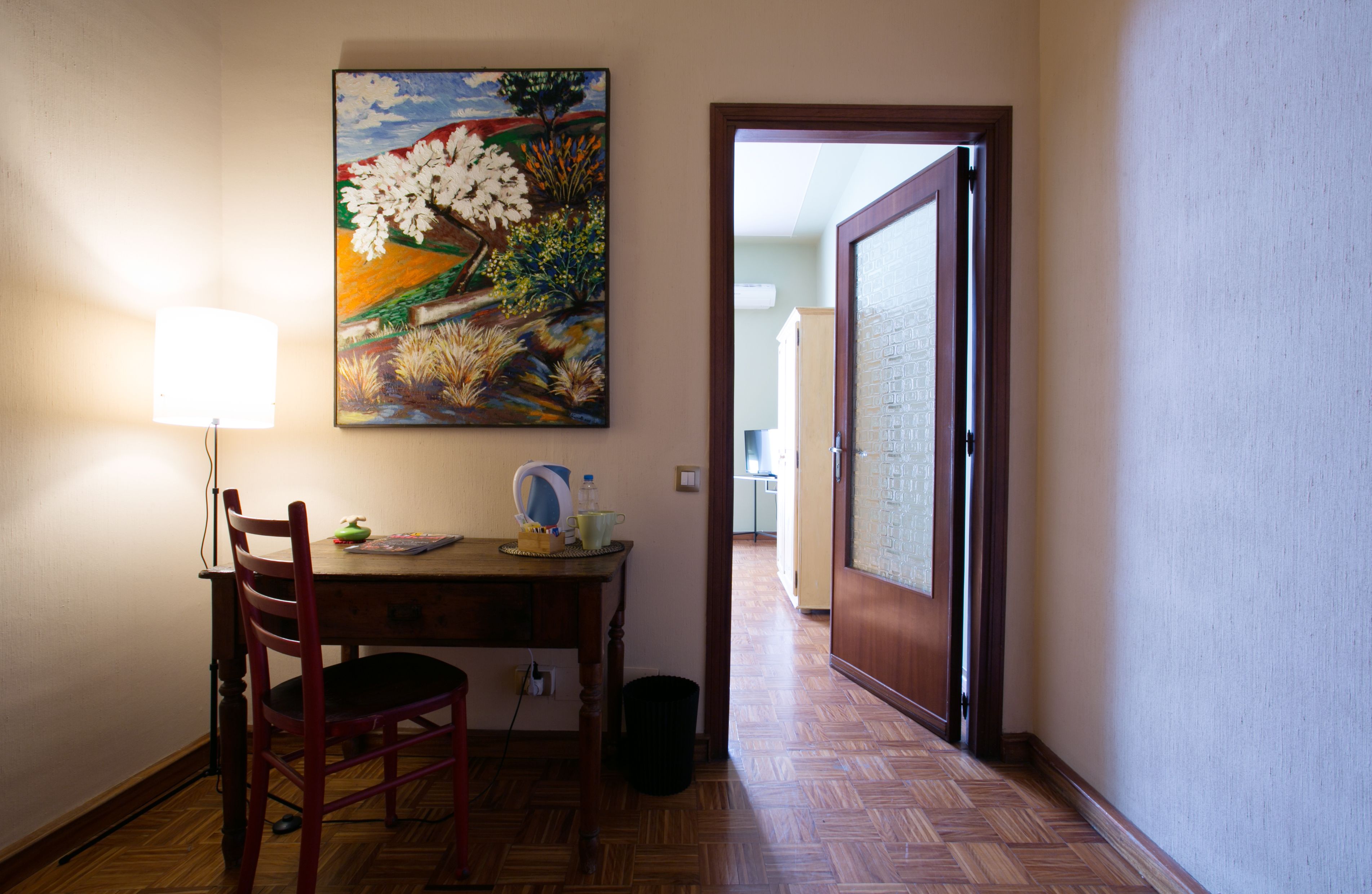 Uma área de jantar com mesa de madeira, uma cadeira, um abajur e um quadro na parede.