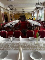 Uma sala de jantar formal com uma mesa comprida posta para refeição, cadeiras estofadas em vermelho e um lustre.