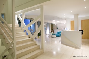 Interior moderno com escada, balcão de recepção e sala de estar com sofá azul.