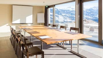 Uma sala de conferências com uma mesa grande, cadeiras, um quadro branco e vista para montanhas cobertas de neve através de grandes janelas.
