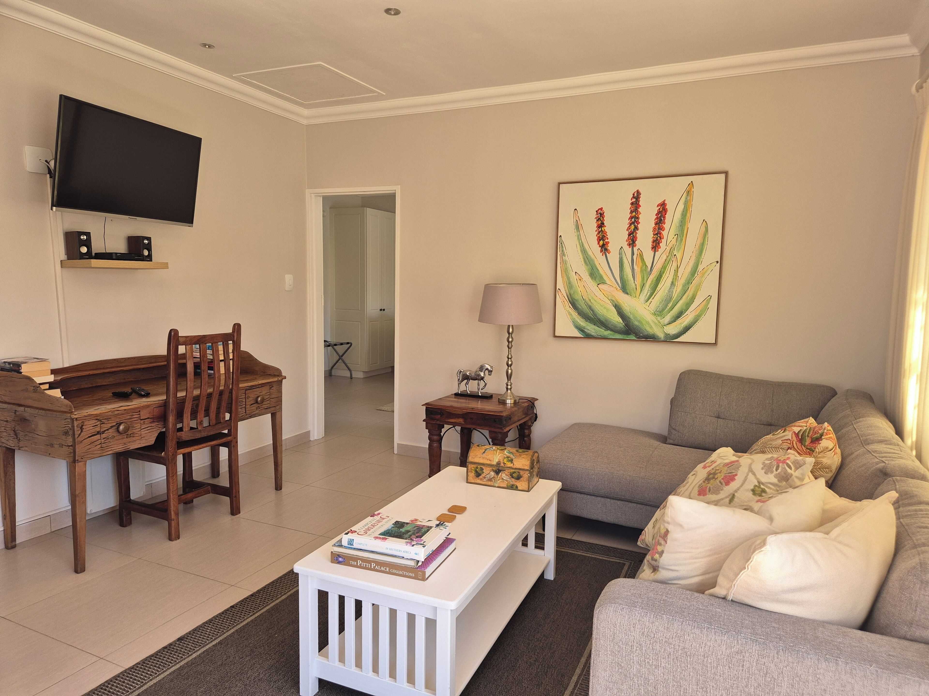 Sala de estar com mesa de jantar de madeira, mesa de centro branca, sofá cinza e televisão fixada na parede.
