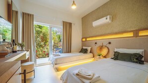 Quarto de hotel com duas camas, uma escrivaninha com cadeira, uma janela grande com cortinas e um aparelho de ar condicionado.