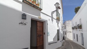 Uma rua estreita com um edifício branco, porta de madeira e uma placa com a inscrição 'Casa Shelly Hospedaria'.