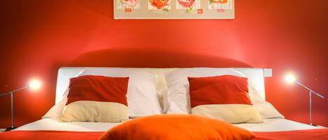 Cama com roupa de cama vermelha e branca, dois travesseiros vermelhos e um travesseiro laranja.
