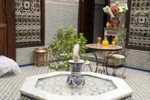 Uma fonte com design azul e branco, rodeada por azulejos estampados e uma pequena mesa com bebidas.