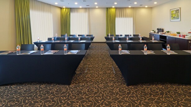 Uma sala de conferência com uma mesa comprida, cadeiras, garrafas de água e um espaço para café.