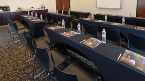 Uma sala de conferências com mesas, cadeiras, garrafas de água e folhetos informativos.