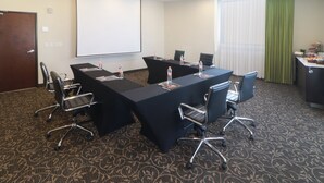 Uma sala de conferências com uma mesa comprida, cadeiras, tela de projetor e um bebedouro.