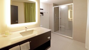 Uma casa de banho moderna com um espelho grande, uma pia, um chuveiro e uma sanita.