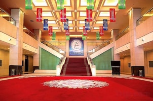 Um saguão de hotel com tapete vermelho, um relógio e uma escada que dá acesso aos andares superiores.