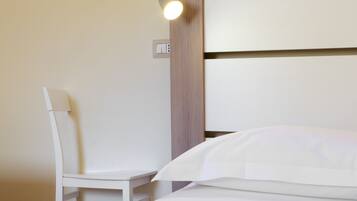 Cama bem arrumada com lençóis brancos, mesa de cabeceira e luminária fixa na parede.