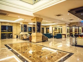 Um hall amplo com piso de mármore polido, uma coluna central e áreas de estar.