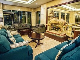 Um hall de hotel com um amplo sofá, uma mesa de centro e uma estátua de um cavalo.