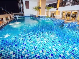 Piscina com azulejos de mosaico azul, rodeada por um edifício com varandas e grandes janelas.