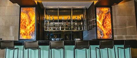 Uma área de bar com um balcão comprido, vários bancos altos e prateleiras repletas de garrafas.