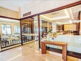 Um saguão moderno de hotel com divisória de vidro, um banco de madeira e um vaso de flores.