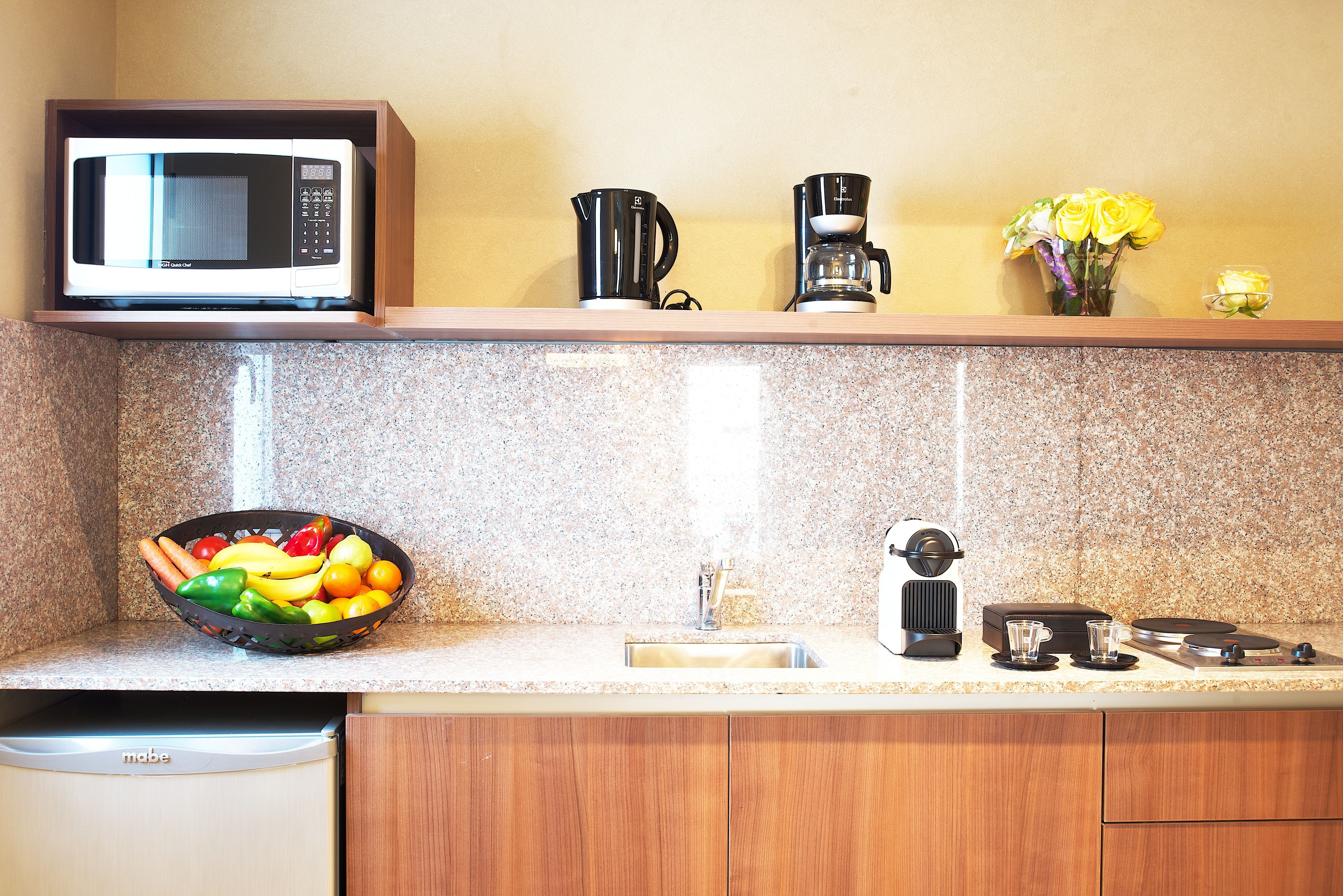 Cozinha com micro-ondas, cafeteira e uma fruteira.