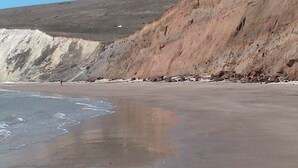 Uma praia com um penhasco íngreme e céu claro.