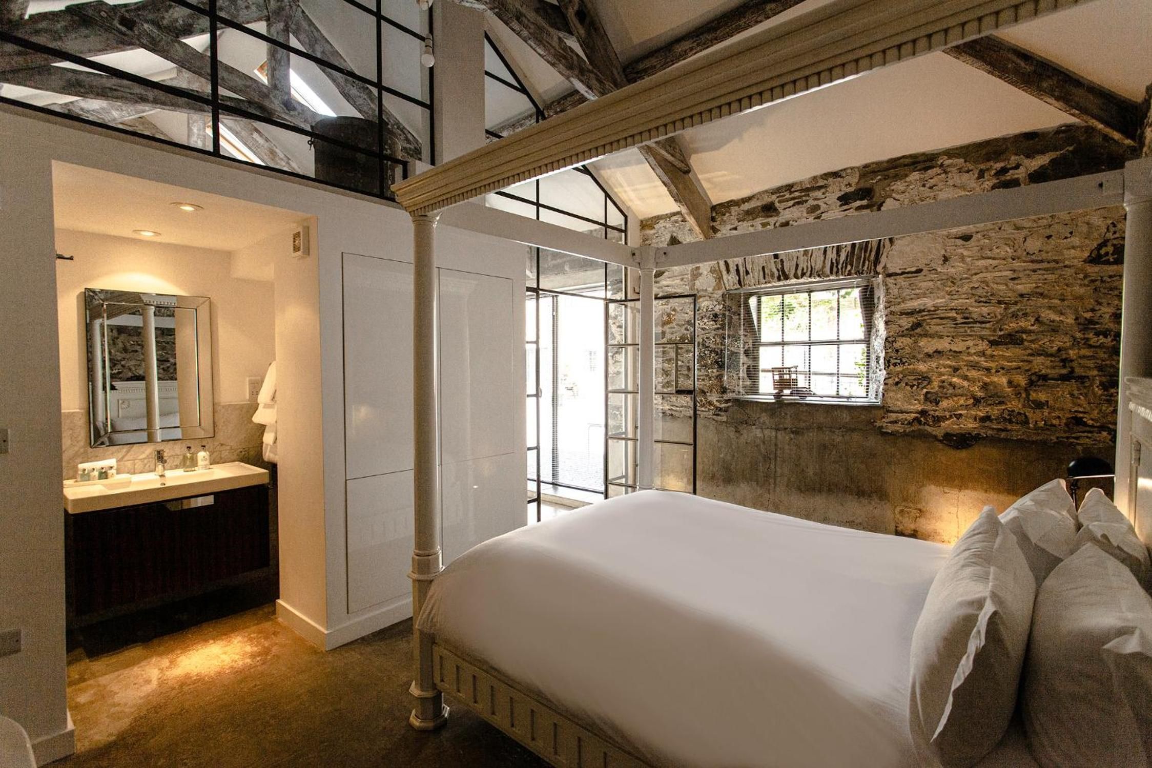 Quarto com cama de dossel, espelho grande, parede de pedra e janela.