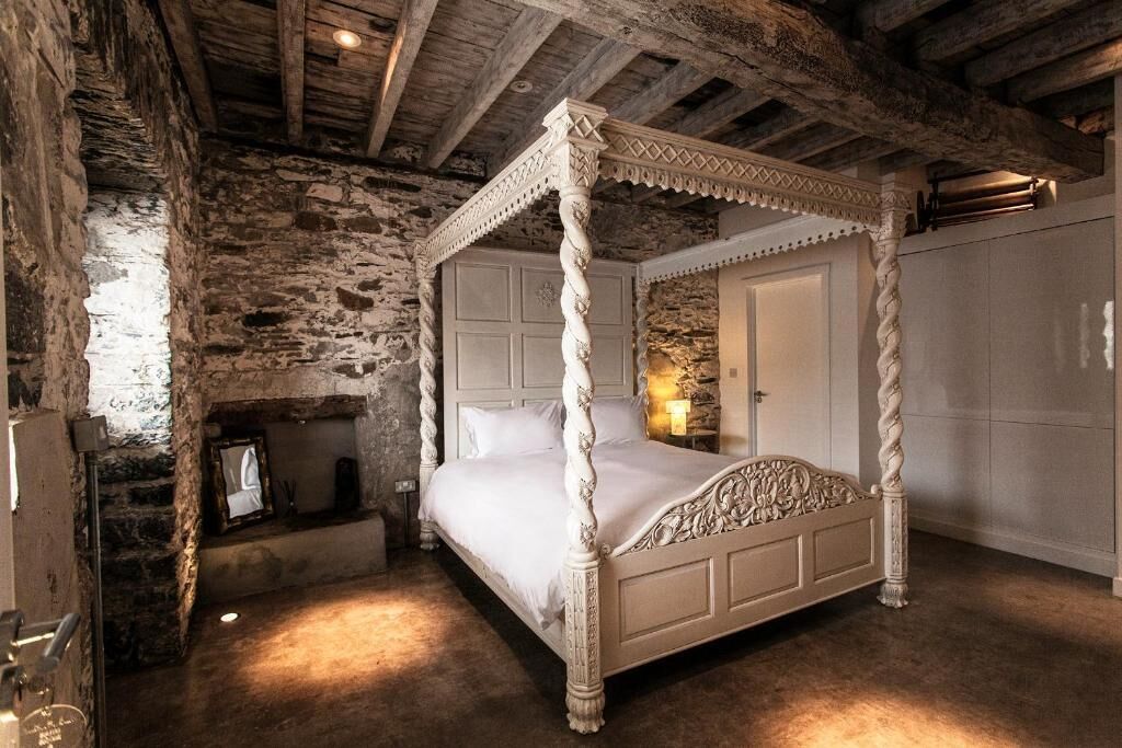 Cama com dossel em quarto com paredes de pedra, teto de madeira e armário branco.