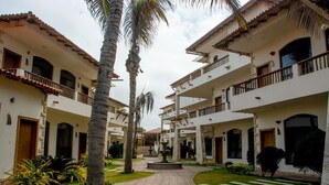 Um pátio central com uma fonte, cercado por edifícios de vários andares com varandas e uma palmeira.