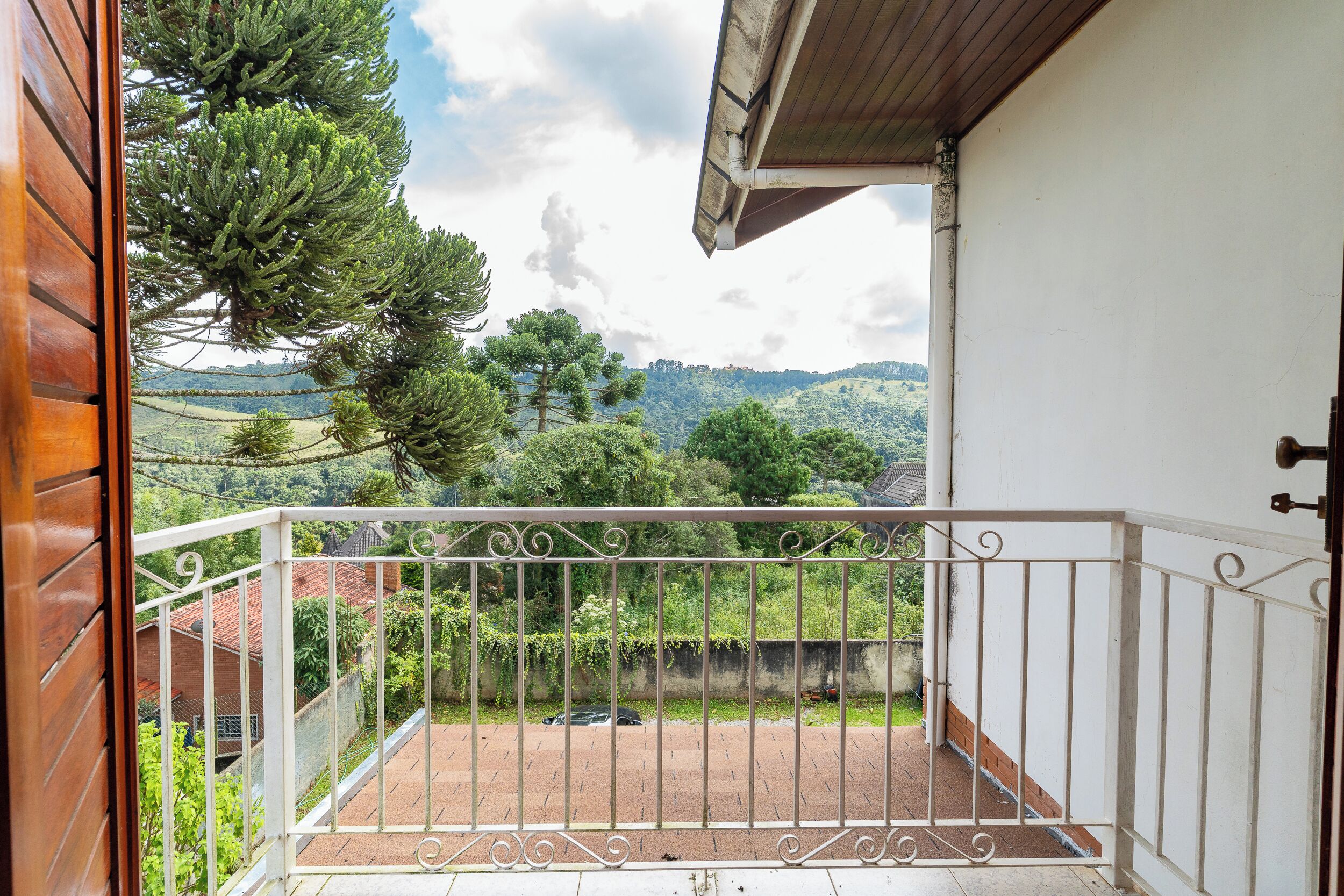 Uma varanda com guarda-corpo de metal, vista de uma paisagem verde e um edifício ao fundo.