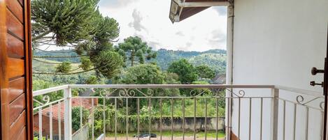 Uma varanda com guarda-corpo de metal, vista de uma paisagem verde e um edifício ao fundo.