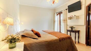 Quarto com cama, luminárias de cabeceira, televisão e janela com cortinas.