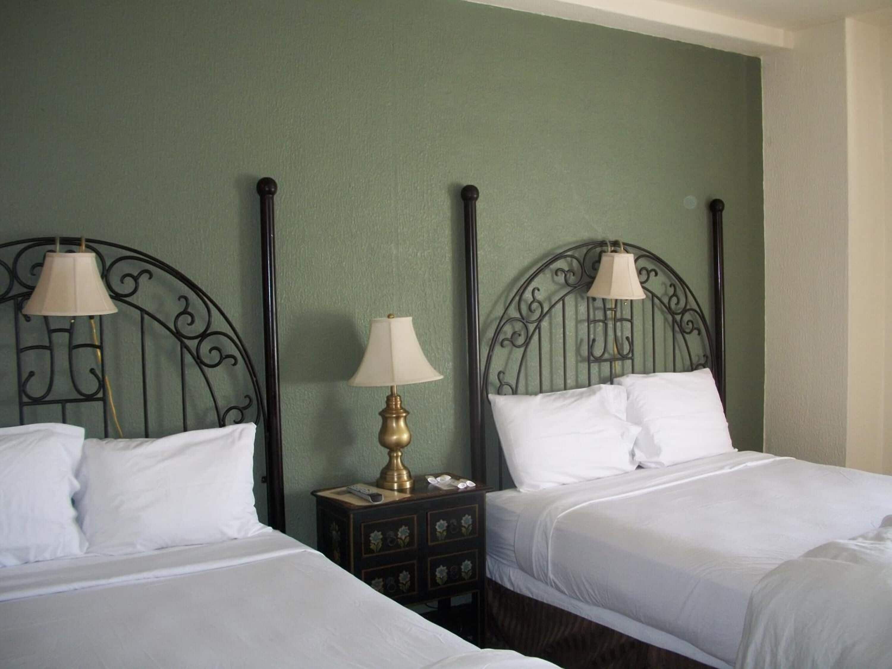 Quarto com duas camas, cada uma com cabeceira e mesa de cabeceira com luminária.