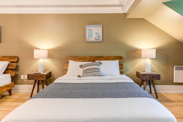 Um quarto bem arrumado com uma cama grande, duas mesas de cabeceira com abajures, um quadro emoldurado na parede e uma cabeceira de madeira.
