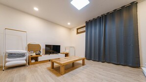 Uma sala de estar moderna com uma mesa de centro de madeira, uma TV de tela plana, um sofá, uma mesinha lateral e uma janela com cortinas.