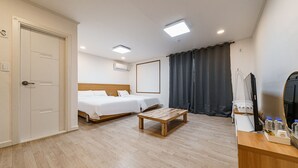 Quarto de hotel com piso de madeira, uma cama, mesa de cabeceira, escrivaninha com espelho e televisão.