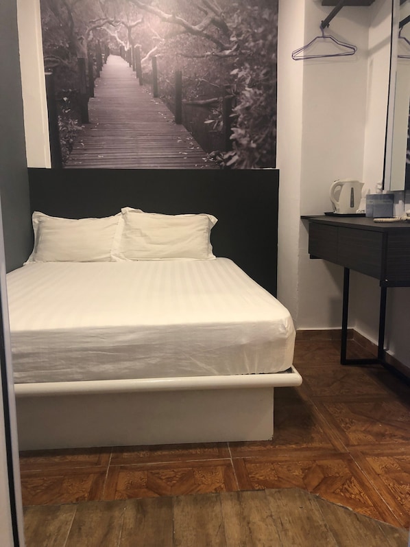 Quarto com cama, piso de madeira, escrivaninha com espelho e cabide fixado na parede.