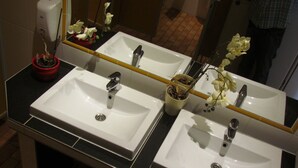 Casa de banho com duas pias, um espelho e um vaso de flores vermelho.