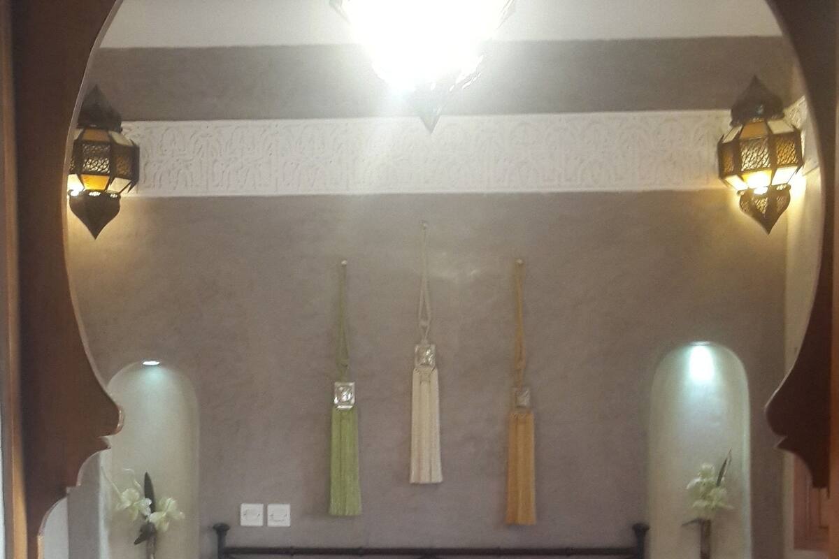 Uma cama com colcha rosa, cabeceira e luminária no teto.