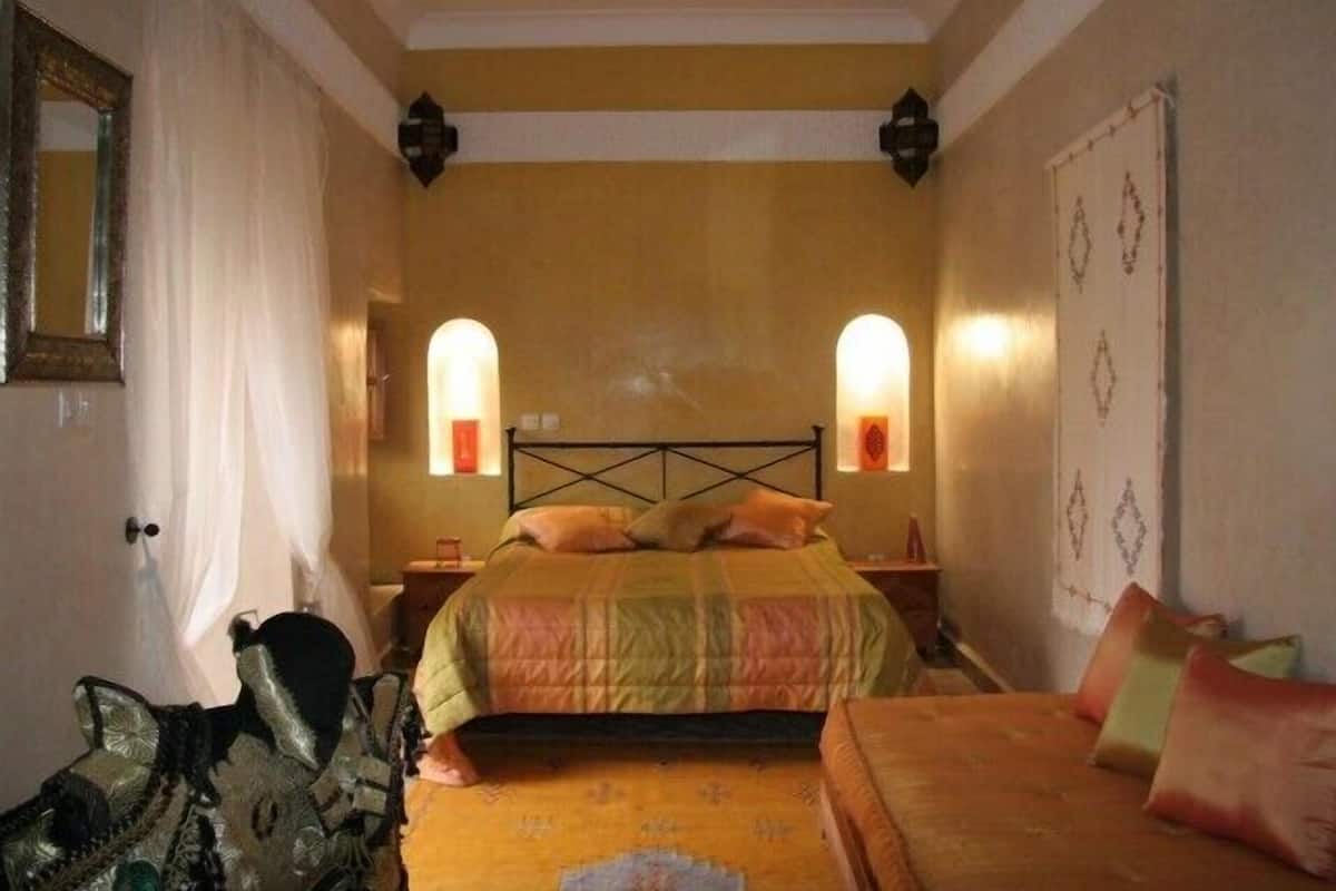 Quarto com cama, duas luminárias de cabeceira, um espelho e parede estampada.