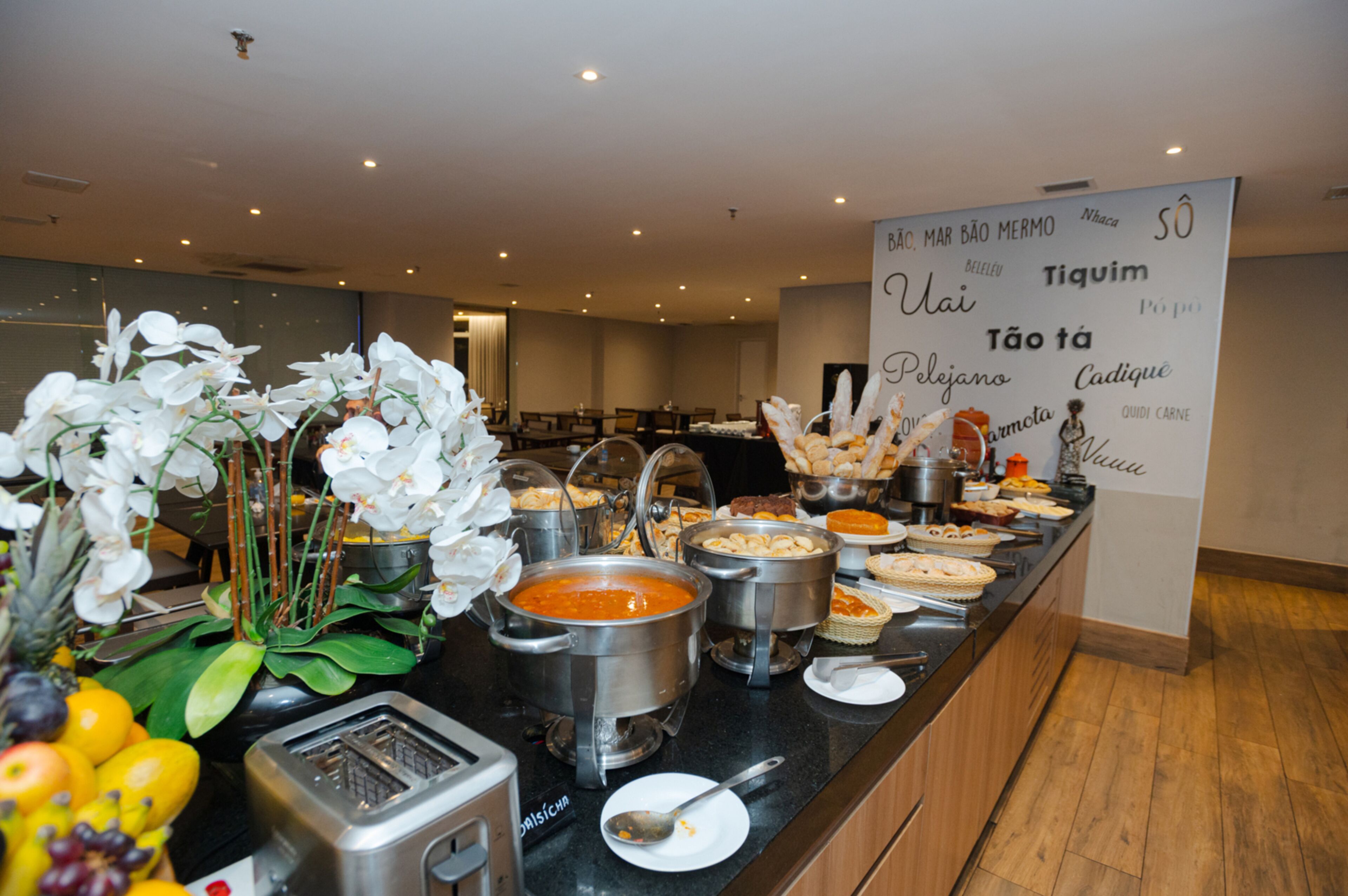 Uma área de buffet com diversos tipos de comida e um letreiro listando o cardápio em português.