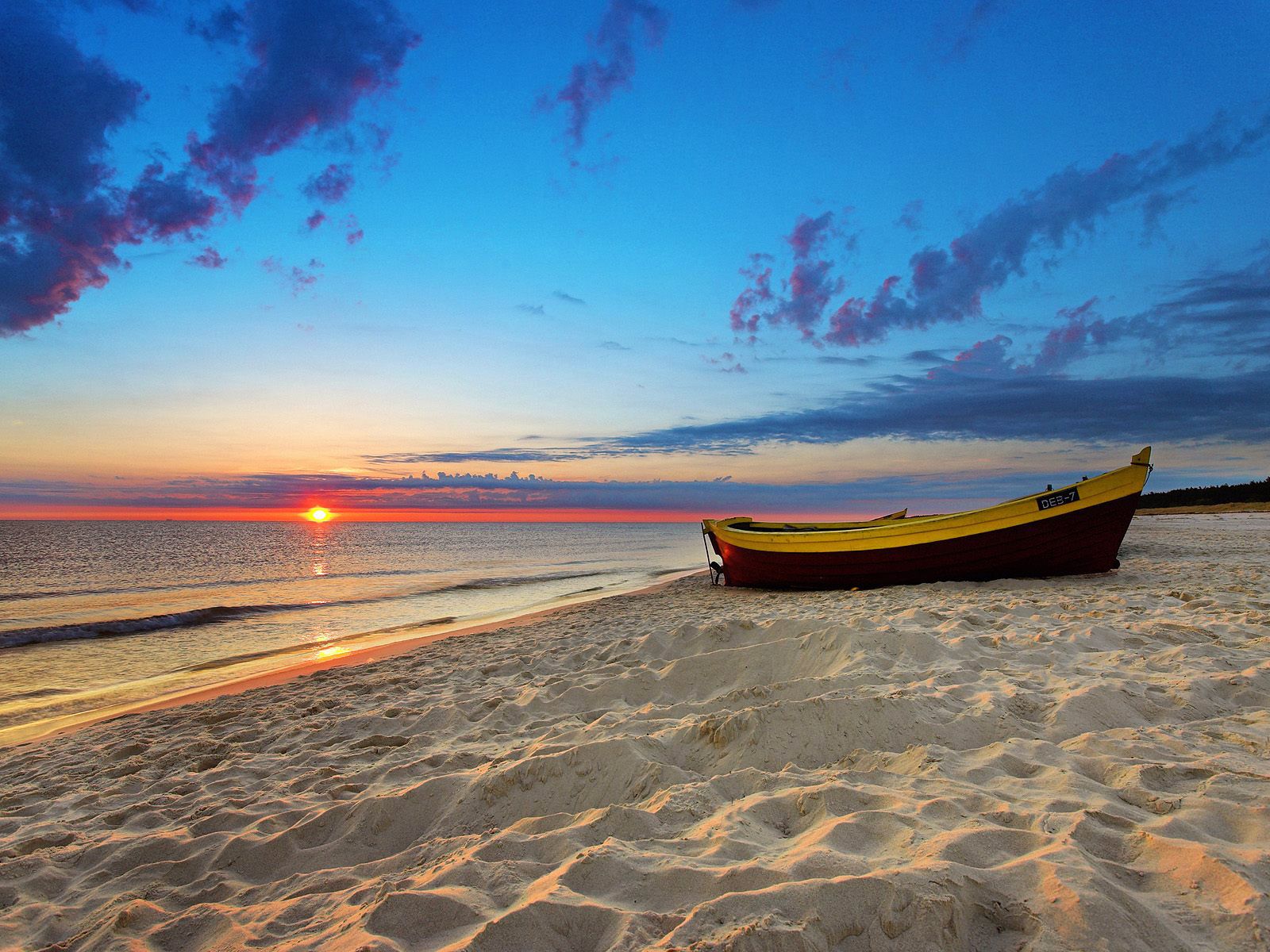 Um barco numa praia arenosa com o pôr do sol ao fundo.