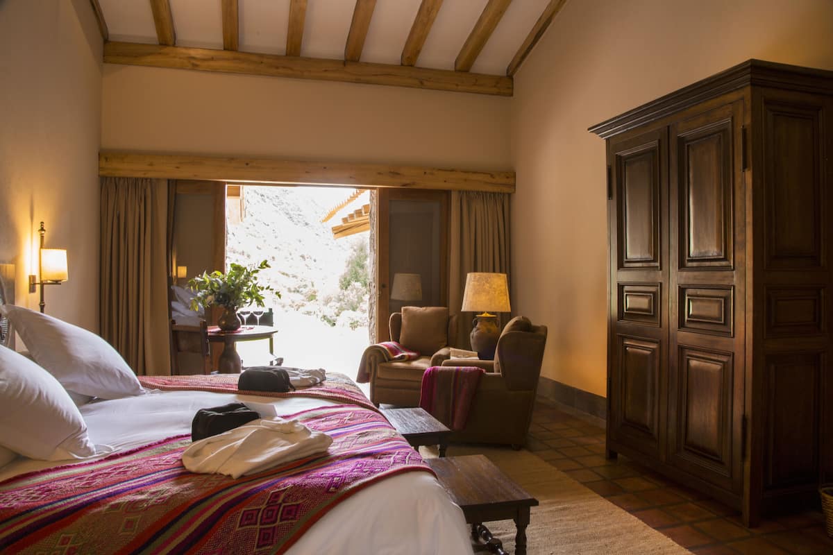 Quarto de hotel com uma cama grande, um guarda-roupa de madeira, uma secretária com uma lâmpada e vista para o exterior.