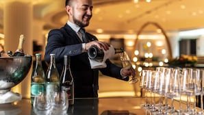 Um bartender servindo champanhe em copos em um bar com garrafas de vinho e uma grande tigela de gelo.