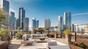 Terraço no telhado com área de estar ao ar livre, plantas em vasos e vista para o horizonte urbano.