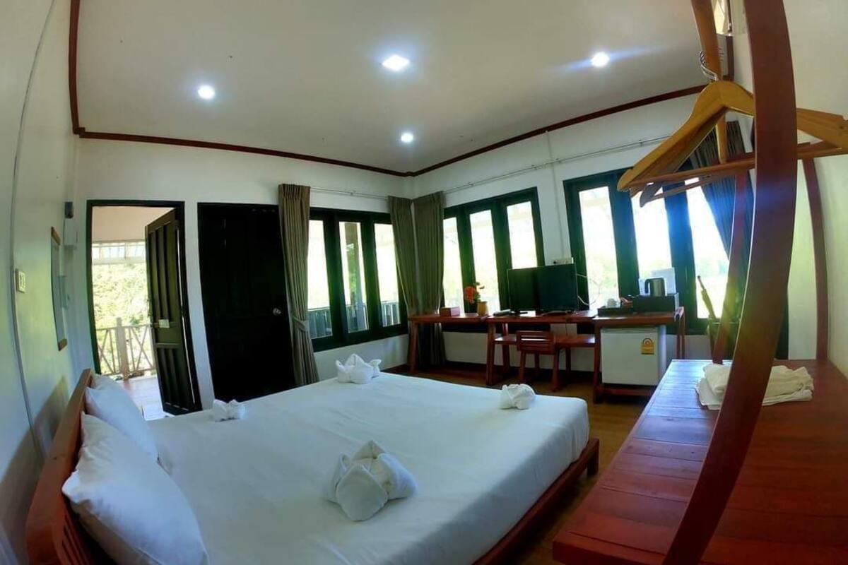 Quarto de hotel com uma cama grande, uma escrivaninha e uma cadeira. Há uma janela com cortinas e uma porta que dá para uma área externa.