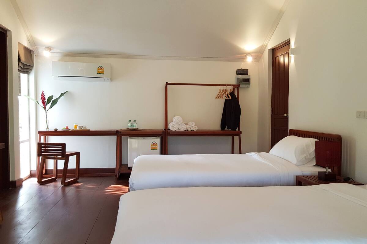 Quarto de hotel com duas camas, uma escrivaninha, uma cadeira, um frigorífico pequeno e ar condicionado fixado na parede.