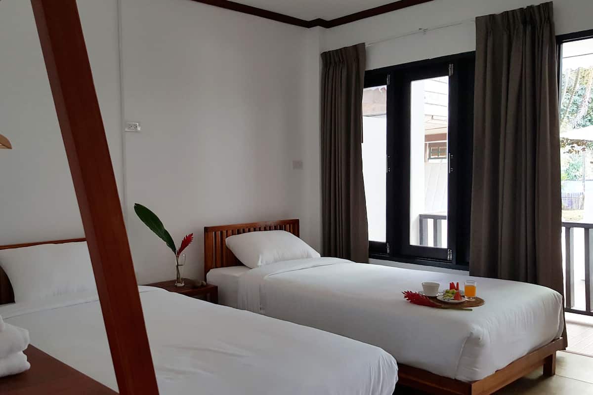 Quarto de hotel com duas camas de solteiro, um guarda-roupa de madeira, uma mesa de cabeceira com um vaso e uma janela com cortinas.